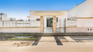Um edifício com entrada protegida por portão, uma pequena área coberta e um caminho pavimentado até o portão.