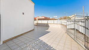 Uma área externa ampla com piso de azulejos, parede branca e cerca de metal.