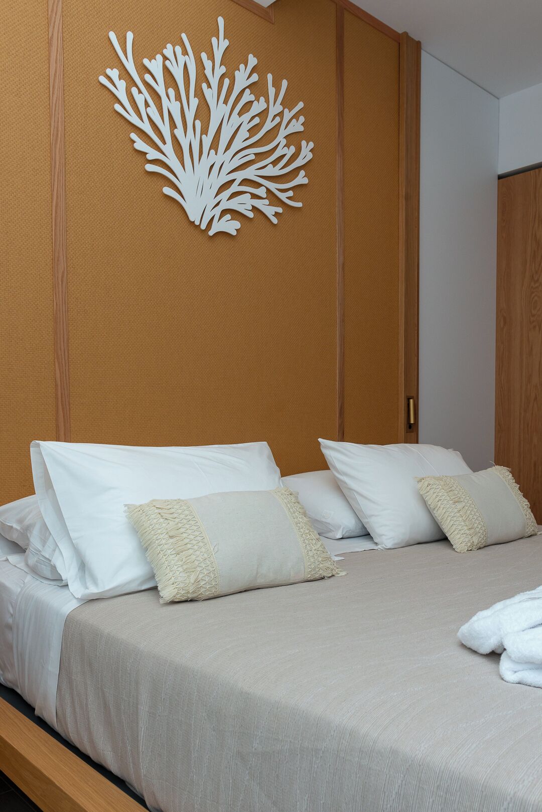 Quarto de hotel com cama, roupa de cama branca e um objeto decorativo na parede.