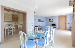 Uma sala de estar moderna com uma mesa de jantar de vidro, cadeiras brancas, uma televisão e obras de arte na parede.