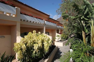 Hotel com área externa coberta, vasos de plantas e montanhas ao fundo.