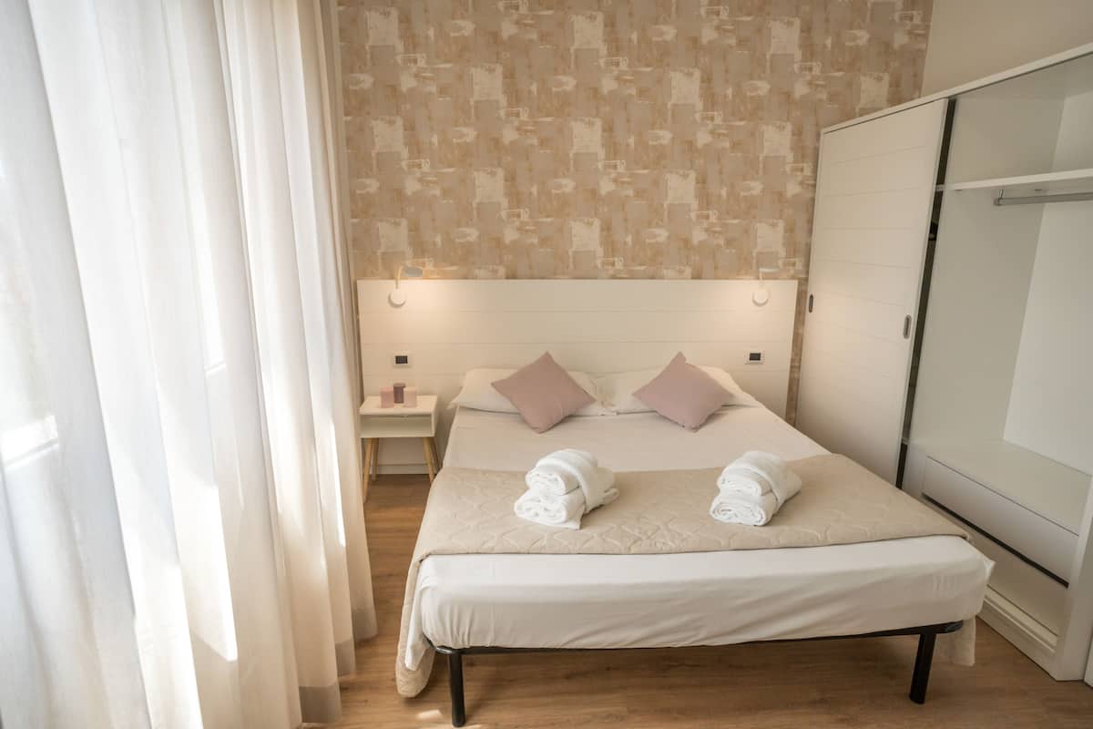 Quarto de hotel bem arrumado, com cama, mesas de cabeceira e guarda-roupa.