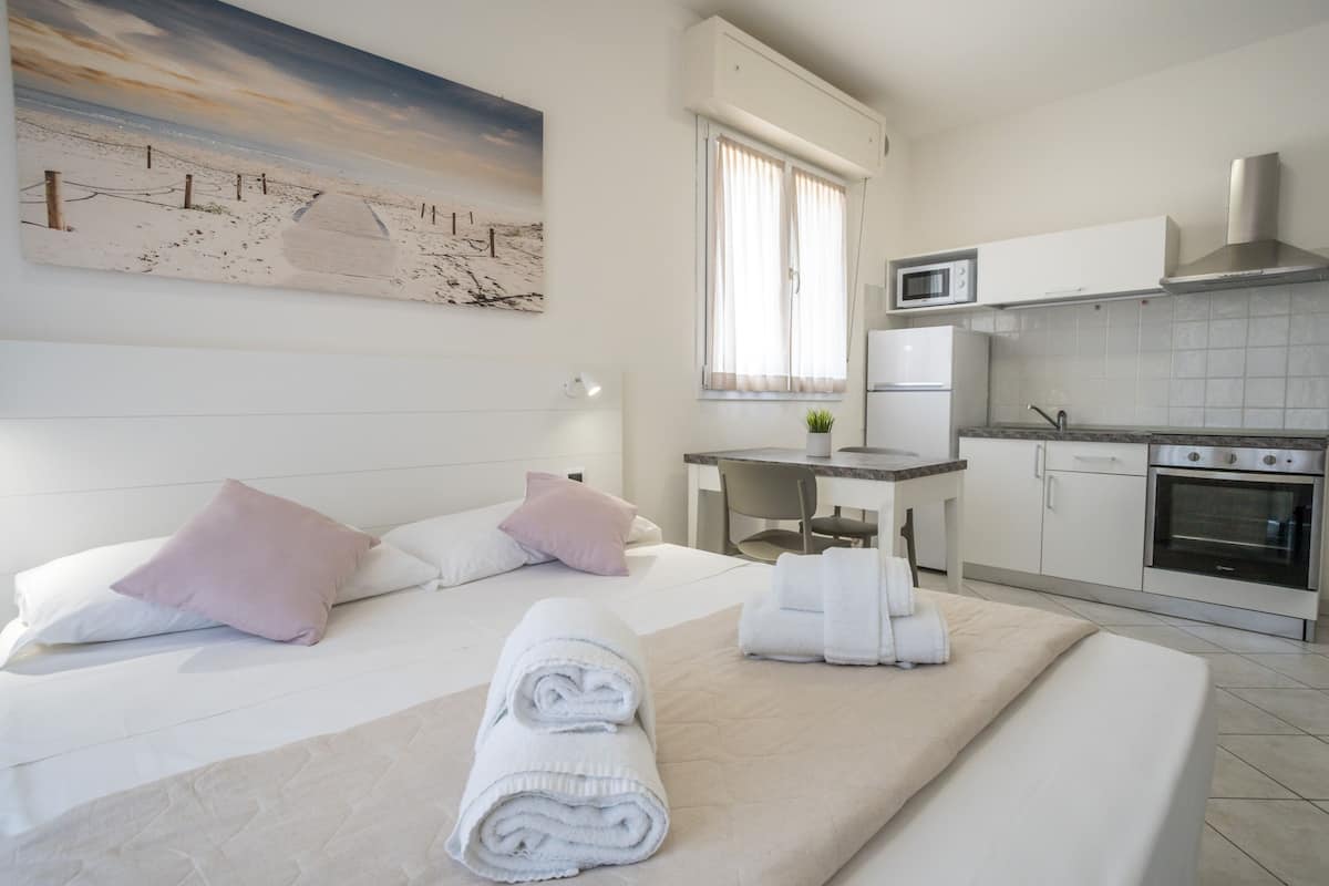 Quarto de hotel com uma cama, escrivaninha, cadeira, micro-ondas, fogão e uma grande pintura na parede.