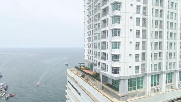 Um edifício alto com vários andares, grandes janelas e vista para o mar.
