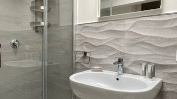 Casa de banho com cabine de duche em vidro, lavatório branco com uma torneira e parede com textura atrás do lavatório.