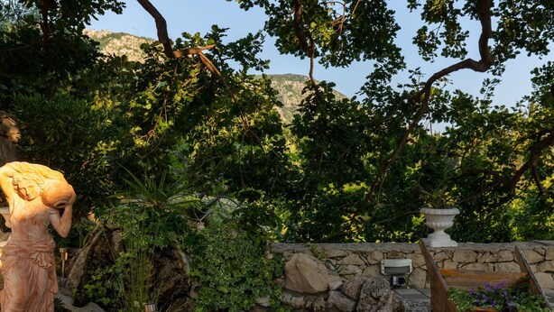 Um jardim com uma estátua, um muro de pedra e um pequeno elemento aquático.