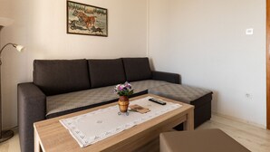 Uma sala de estar com um sofá cinzento, uma mesa de centro de madeira com um vaso de flores, um abajur e um quadro na parede.