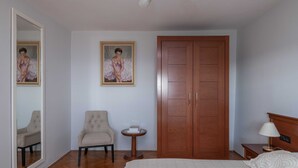 Quarto com cama, guarda-roupa de madeira, cadeira, mesa redonda pequena e duas molduras na parede.