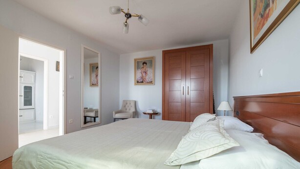Quarto com uma cama grande, um guarda-roupa de madeira, uma cadeira e uma mesa pequena.