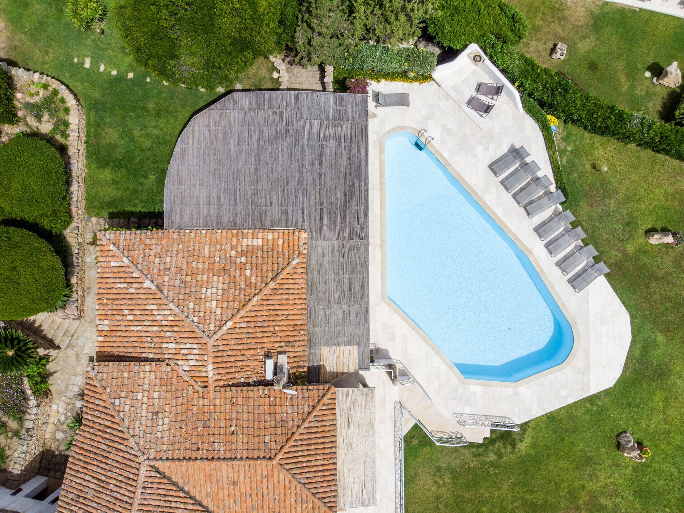 Vista aérea de uma propriedade com piscina, área de varanda coberta e telhado de pedra.