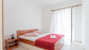 Quarto individual com uma cama e cabeceira de madeira, mesa de cabeceira com abajur e janela com cortinas.