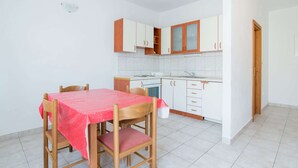 Uma cozinha compacta com armários brancos, uma mesa vermelha e uma cadeira de madeira.