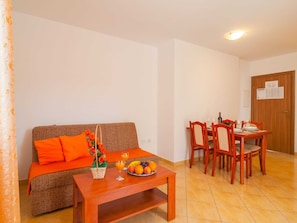 Uma sala de estar com sofá, mesa de centro com frutas, e uma área de jantar com cadeiras e mesa.