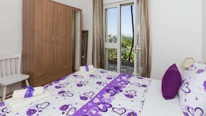 Quarto com cama, guarda-roupa, janela com cortinas e vista para o verde lá fora.