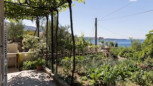 Um jardim com um caminho de pedra que leva a um espaço de estar, cercado por vegetação exuberante e vista para o mar.