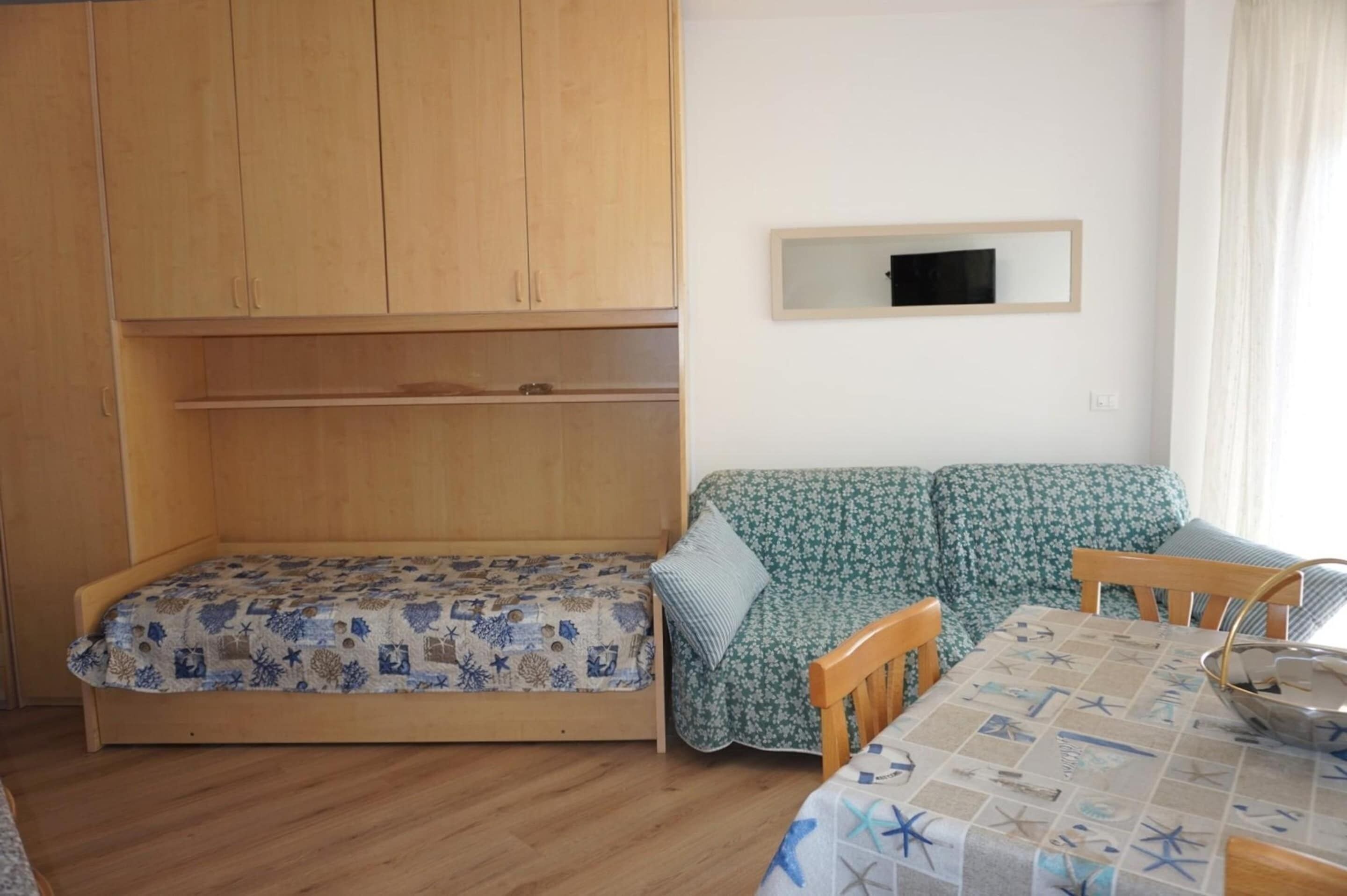 Quarto com cama de madeira, um sofá, uma mesa com toalha de mesa estampada e um espelho fixado na parede.