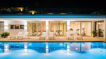 Um edifício moderno com piscina, portas de vidro que dão para uma área de lounge com cadeiras e equipamentos de ginástica.