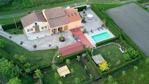 Vista aérea de uma propriedade residencial com piscina, varanda coberta e gramado bem cuidado.