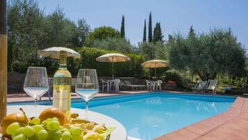 Uma área na piscina com uma mesa posta, incluindo uma garrafa de vinho, copos e uma cesta de frutas.