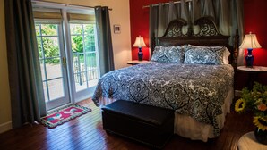 Quarto com cama grande, duas mesinhas de cabeceira com luminárias, um banco e vista através de uma porta de vidro.