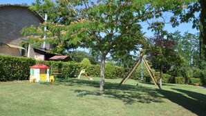 Um jardim bem cuidado, com balanço, uma casinha de brincar e uma mesa de piquenique.