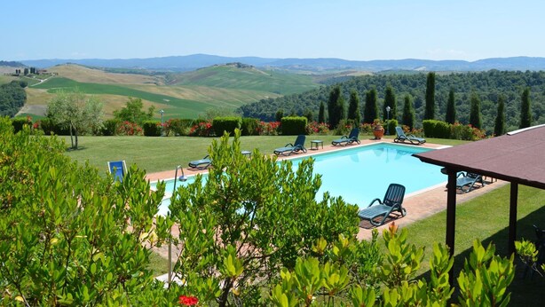 Área de piscina com espreguiçadeiras, cercada por vegetação e colinas ao fundo.
