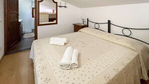 Quarto com cama, mesa de cabeceira, espelho e porta que dá para outro ambiente.
