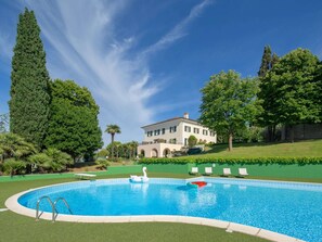 Piscina com um flutuador de cisne e um círculo inflável vermelho, rodeada por grama bem cuidada e árvores.