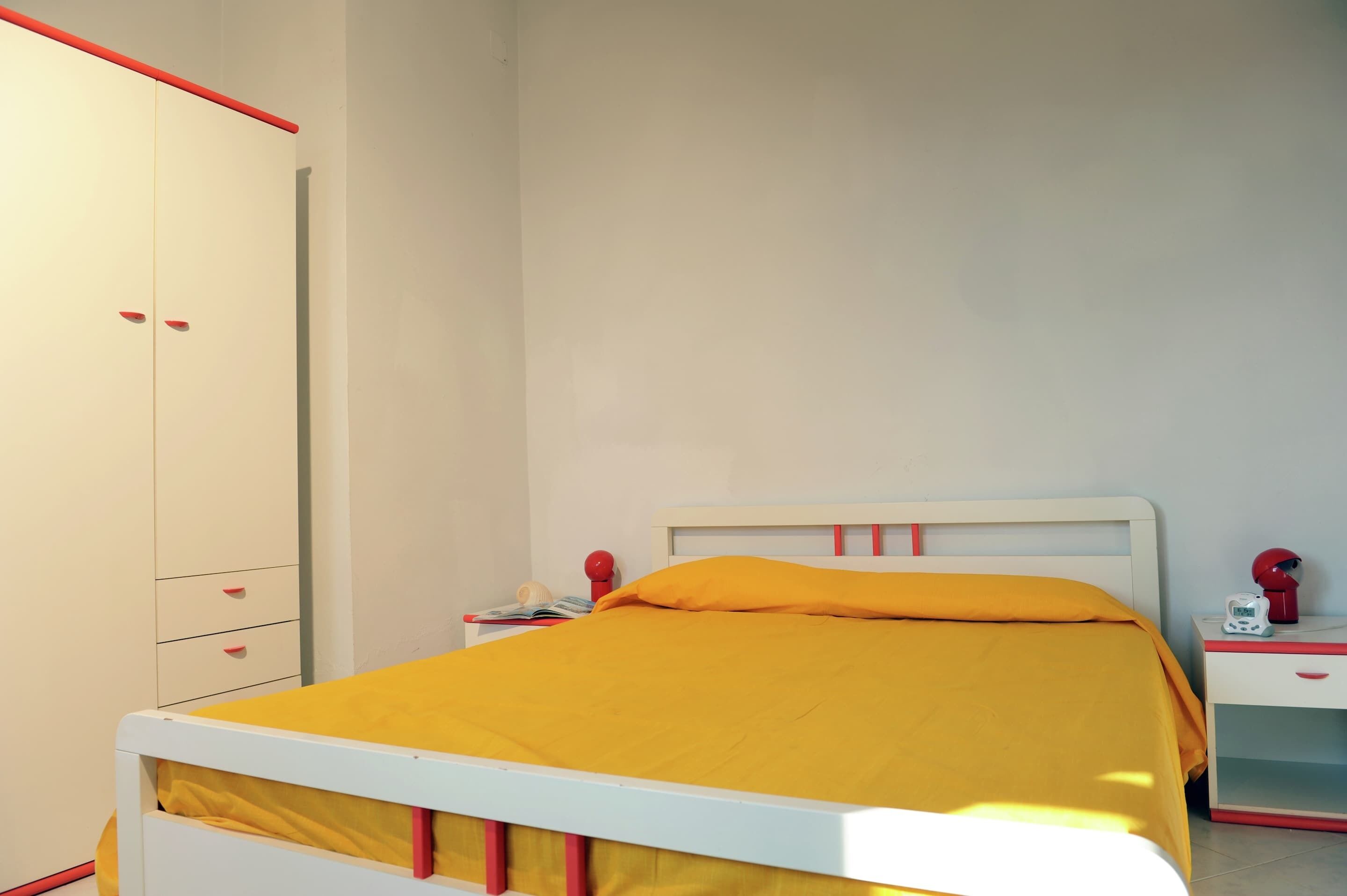 Quarto com cama, mesa de cabeceira, guarda-roupa e escrivaninha.
