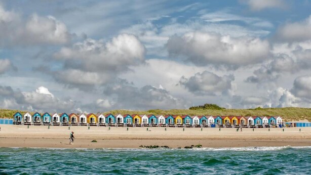 Uma fileira de cabanas coloridas ao longo de uma praia arenosa, com o mar em primeiro plano.