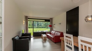 Uma sala de estar moderna com um sofá vermelho, uma mesa de jantar com cadeiras brancas e uma janela grande com vista para o verde.