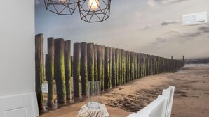 Mesa de jantar com pão e um centro de mesa em vidro, um mural na parede retratando uma cerca de madeira e árvores, e duas luminárias pendentes geométricas.
