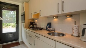 Cozinha moderna com armários brancos, eletrodomésticos de aço inoxidável e janela com vista para o verde.