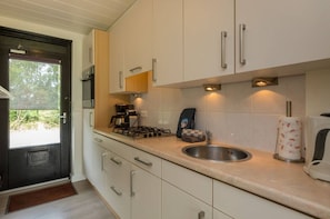 Cozinha moderna com armários brancos, eletrodomésticos de aço inoxidável e janela com vista para o verde.