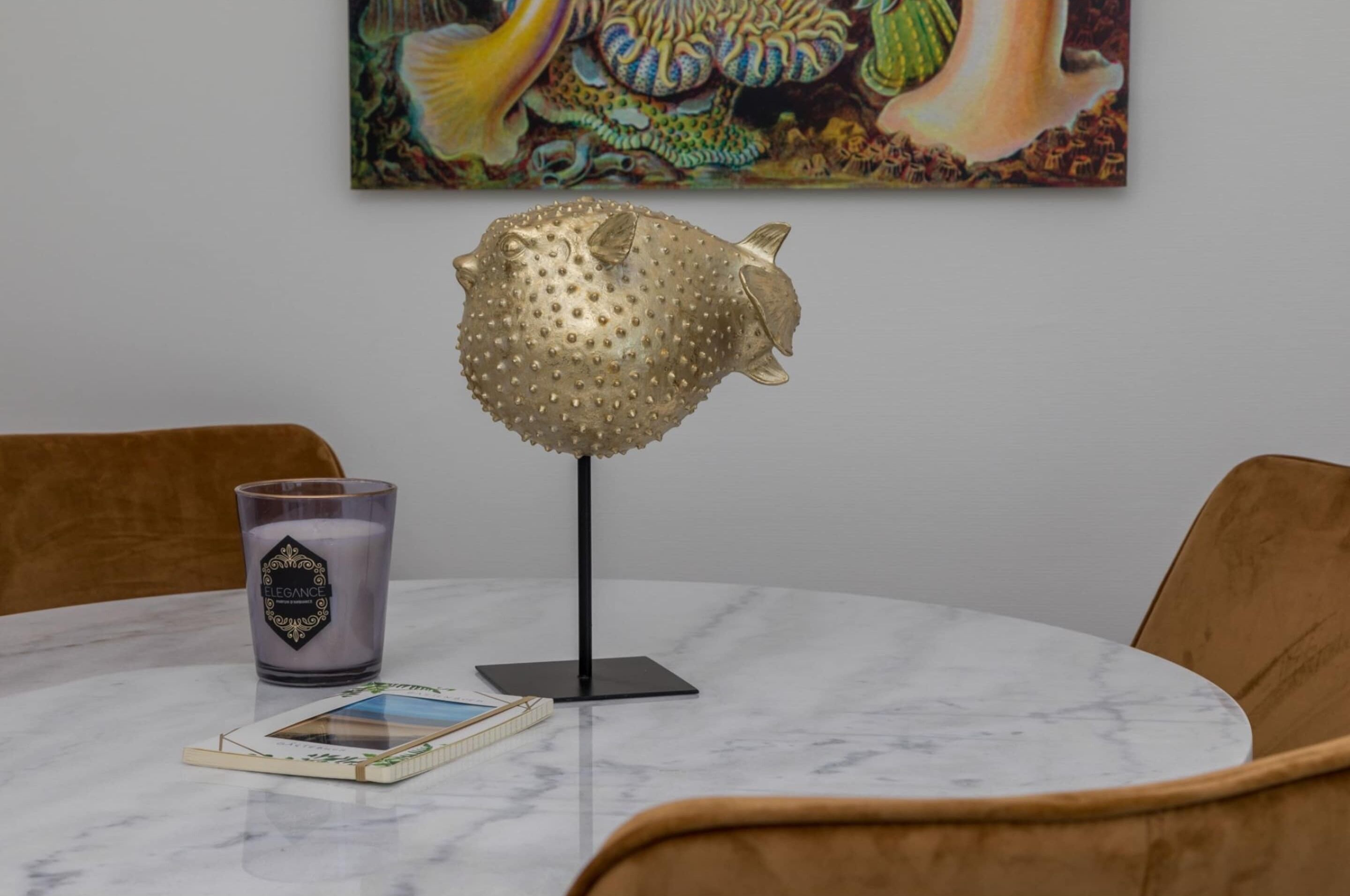 Uma mesa redonda de mármore com uma escultura de baiacu, uma vela e um livro.