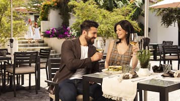 Um casal jantando em mesa ao ar livre, com vista para um jardim e degraus.