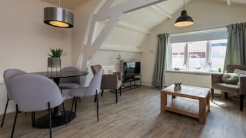 Uma sala de estar moderna com área de jantar, piso de madeira e janelas amplas.