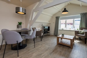 Uma sala de estar moderna com área de jantar, piso de madeira e janelas amplas.