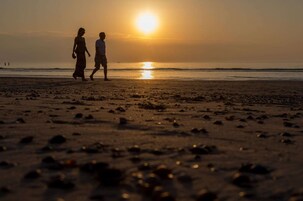 Uma praia com duas pessoas caminhando em direção ao pôr do sol.
