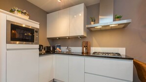 Uma cozinha moderna com armários brancos, micro-ondas embutido, fogão a gás e exaustor de aço inoxidável.