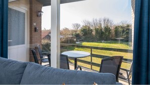 Uma varanda com mesa e cadeiras, vista para um gramado verde e um muro de tijolos.