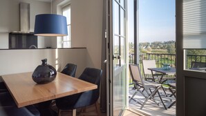 Uma sala de jantar moderna com uma mesa de madeira, cadeiras pretas e uma luminária pendente azul. Uma janela grande oferece vista para o exterior.
