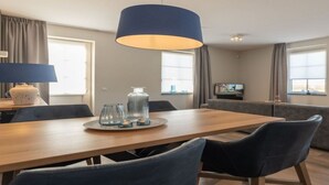 Quarto de hotel moderno com área de refeições, sofá e televisão.