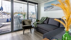 Uma sala de estar moderna com um sofá, uma poltrona e uma grande janela com vista para uma marina.