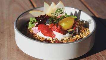 Uma tigela de comida com diversas frutas, nozes e uma colherada de creme sobre uma mesa de madeira.