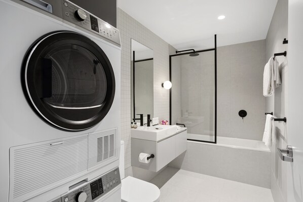 Uma casa de banho moderna com máquina de lavar e secar integradas, toucador com espelho e zona de duche separada.