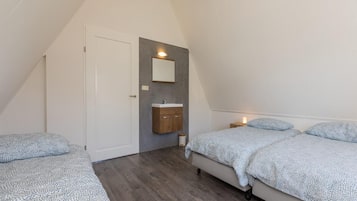 Quarto com duas camas, banheiro pequeno com espelho e pia, e teto inclinado.