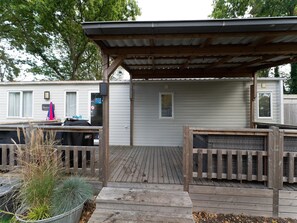 Uma área externa coberta com deck de madeira, churrasqueira e um pequeno galpão.