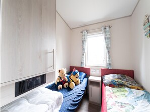 Quarto com duas camas, uma janela com cortinas, um guarda-roupa e um urso de pelúcia em uma das camas.