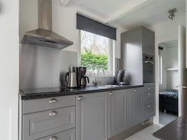 Cozinha moderna com armários cinza, coifa de aço inoxidável, cafeteira e janela com vista para o verde.